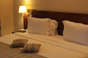 Quarto de hotel com cama bem arrumada, almofadas listradas, luminária de cabeceira e cabeceira de madeira.