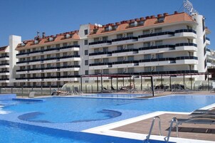 Hotel com várias varandas, piscina e área coberta com cadeiras.