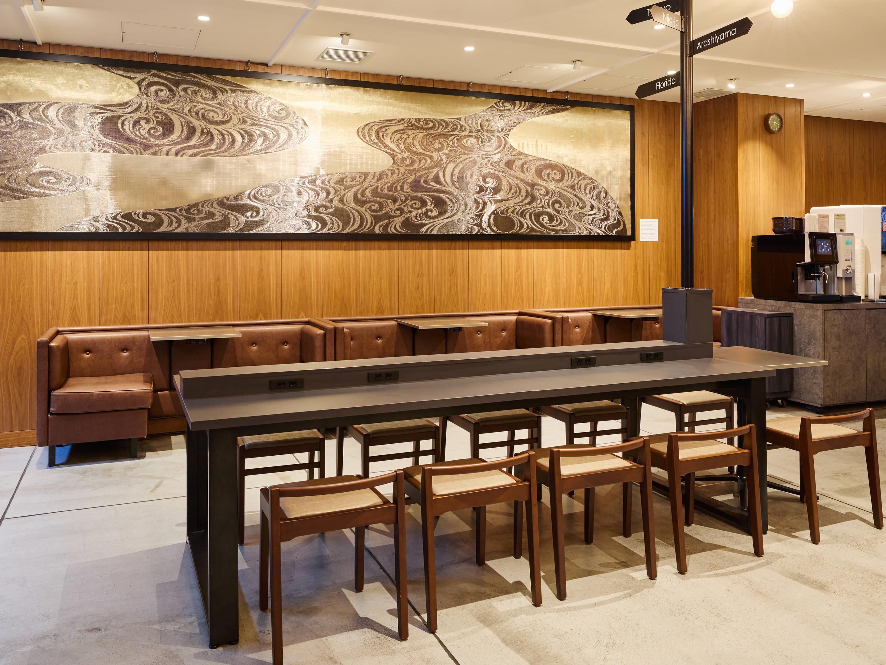 Um saguão de hotel com uma mesa comprida e cadeiras, um relógio e uma máquina de café.