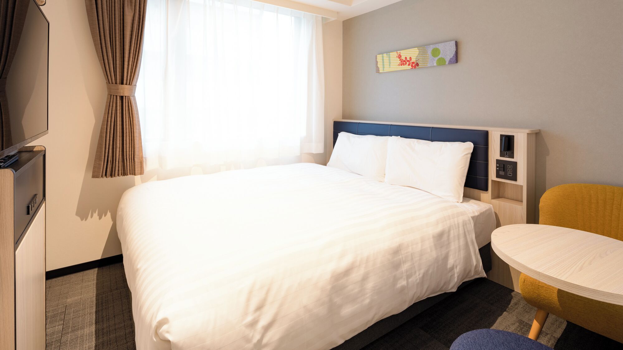 Quarto de hotel com cama, escrivaninha, cadeira, televisão e obra de arte na parede.