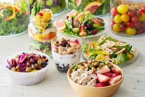 Diversos alimentos como saladas, um copo de parfait de iogurte e uma cesta de frutas.