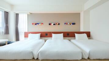 Quarto de hotel com três camas de solteiro, uma mesa redonda pequena e painel de controle fixado na parede.