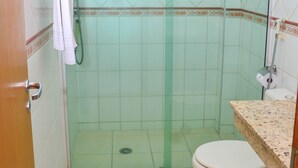 Casa de banho com chuveiro em cabine de vidro, sanita e lavatório com bancada em azulejos.