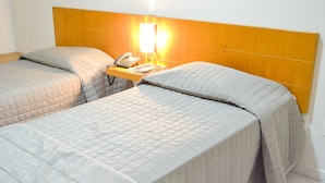 Quarto de hotel com duas camas, uma mesa de cabeceira com abajur e um telefone.
