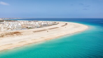 Na praia, espreguiçadeiras, guarda-sóis, prática de windsurfe 