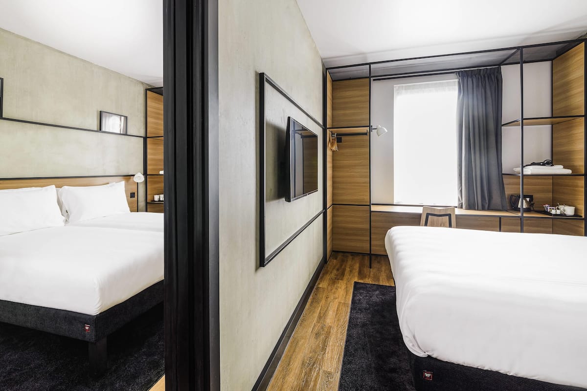 Quarto de hotel com duas camas, televisão, escrivaninha e guarda-roupa.