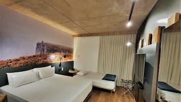 Quarto de hotel com duas camas, um mural grande na parede, uma luminária no teto e uma TV na parede.