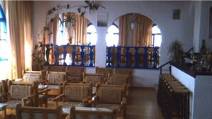 Um hall com cadeiras e mesas de madeira, janelas em arco e plantas em vasos.