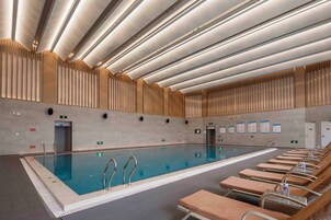 Uma ampla piscina interior com várias pistas, área de estar com espreguiçadeiras e design de teto moderno com iluminação linear.