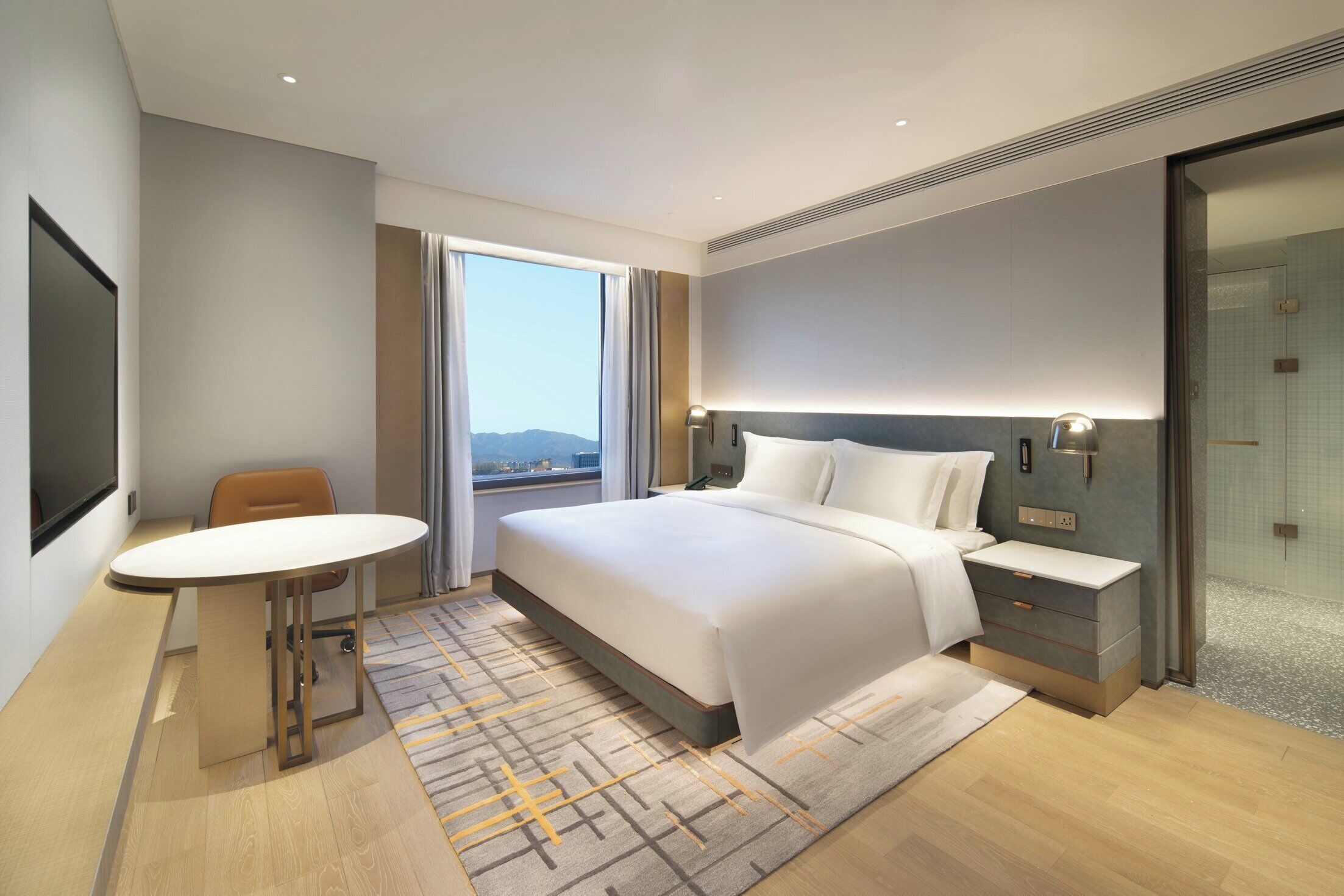 Quarto de hotel moderno com uma cama grande, uma escrivaninha e vista para a cidade.