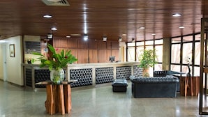 Um hall com balcão de atendimento, assentos acolchoados, mesa de centro e plantas em vasos.