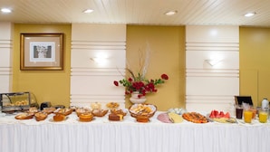 Uma mesa de buffet com diversos alimentos, um quadro na parede e um vaso com flores vermelhas.