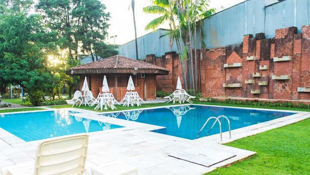 Uma piscina com espreguiçadeiras e guarda-sóis, cercada por uma parede de tijolos e vegetação.
