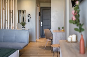 Quarto moderno com sofá cinza, divisória de madeira, mesinha com velas e um vaso de planta.