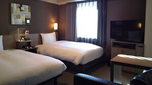 Quarto de hotel com duas camas, televisão, escrivaninha e janela com cortinas.