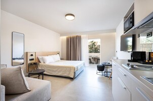 Quarto de hotel moderno com cama, sofá, mesa de jantar e cozinha compacta.