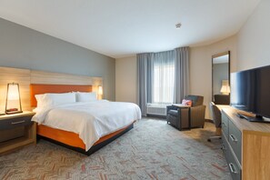 Quarto de hotel com uma cama grande, uma escrivaninha com cadeira, televisão e janela com cortinas.