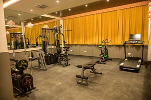 Uma academia com diversos equipamentos de exercício, um espelho e uma esteira.