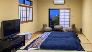 Quarto com uma cama, televisão, mesa pequena e duas cadeiras.