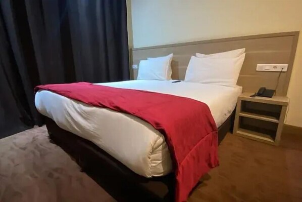 Quarto de hotel com uma cama, mesa de cabeceira e tomada na parede.
