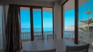 Varanda com mesa e cadeiras, vista para a costa com céu claro e linha de costa distante.