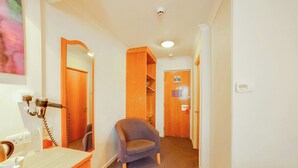 Um corredor estreito com uma cadeira de madeira, um espelho e uma porta com uma placa.