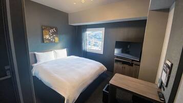 Quarto de hotel com cama, televisão, mesinha e janela com vista para a cidade.