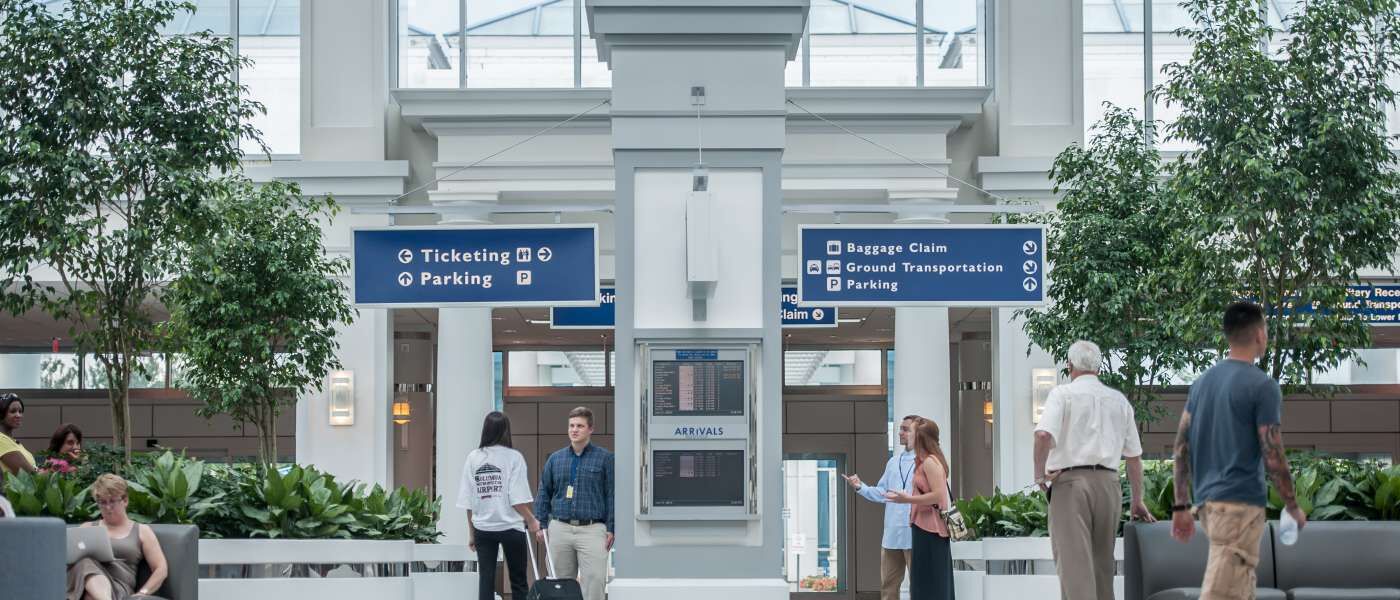 Um terminal de aeroporto com placas de sinalização indicando bilheteria, retirada de bagagem e estacionamento.