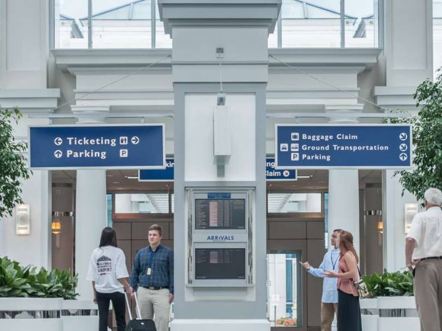 Um terminal de aeroporto com placas de sinalização indicando bilheteria, retirada de bagagem e estacionamento.