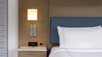 Quarto de hotel com cabeceira de madeira, mesa de cabeceira com luminária e cama com roupa de cama branca.