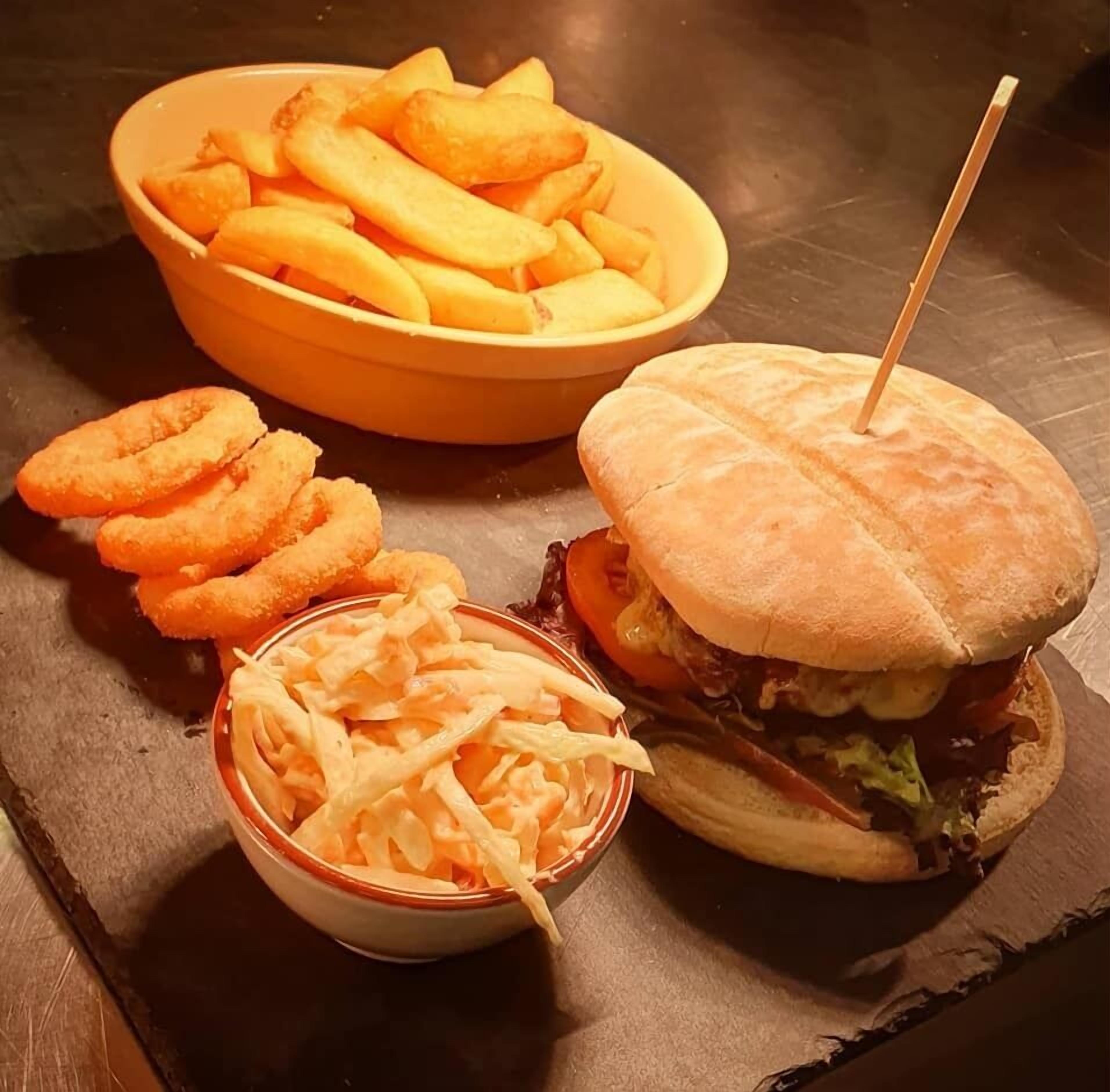 Uma refeição com hambúrguer, batatas fritas, anéis de cebola e salada de repolho.