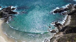 Vista aérea de uma praia com águas turquesas cristalinas, costa rochosa e faixa de areia.