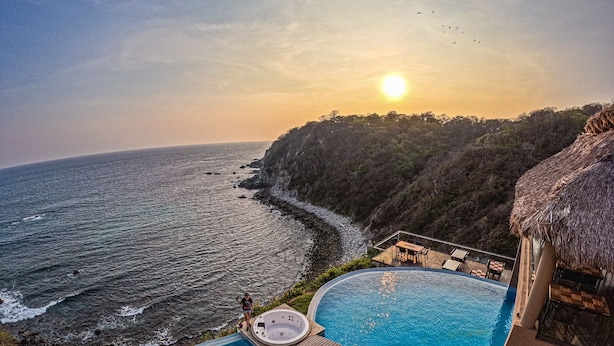 Piscina com hidromassagem e vista para o oceano ao pôr do sol.
