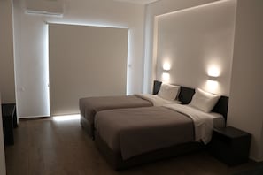 Quarto com duas camas, mesa de cabeceira, luminária na parede.