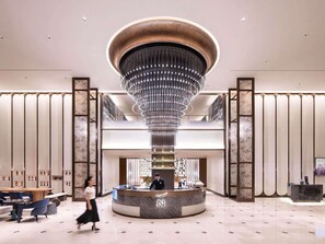 Um hall de hotel com uma grande recepção circular, um lustre central e design moderno com painéis verticais.