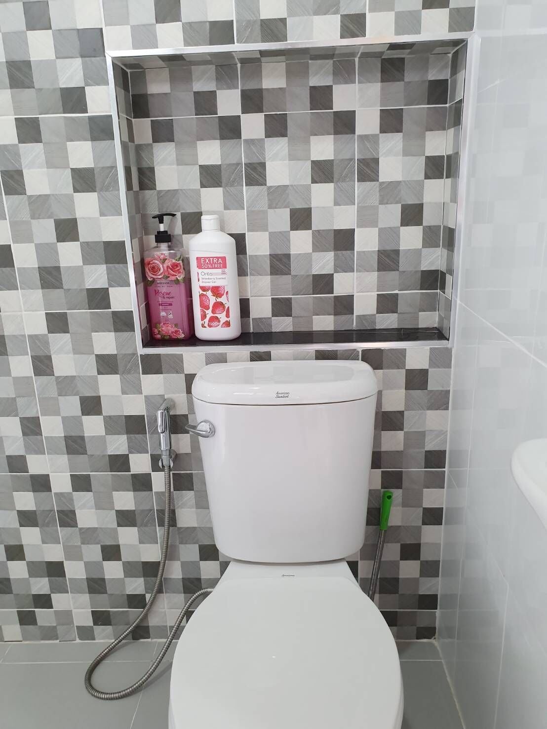 Casa de banho com sanita, chuveiro e prateleira com artigos de higiene pessoal.