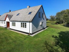 Uma casa térrea com telhado inclinado, porta vermelha e um pequeno jardim.