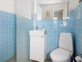 Casa de banho com paredes azulejadas em azul, uma sanita e uma pia branca com torneira.