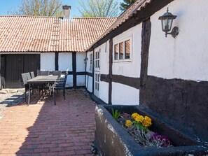 Um edifício tradicional em estilo meio-lenha, com telhado de telhas, um pátio de tijolos e uma mesa com cadeiras.