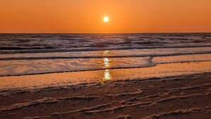 Um pôr do sol sobre o oceano com ondas avançando em direção à praia.