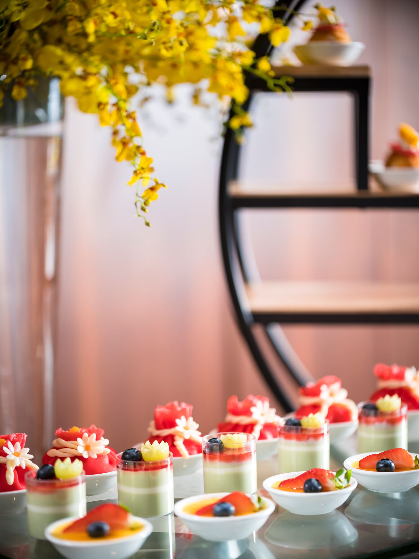 Uma mesa com diversos doces à base de fruta e um vaso com flores amarelas.