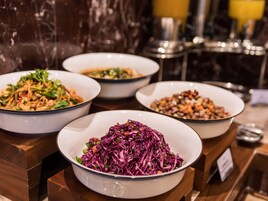 Buffet com diversos pratos, incluindo uma salada de repolho roxo, legumes mistos e um tacho de macarrão.