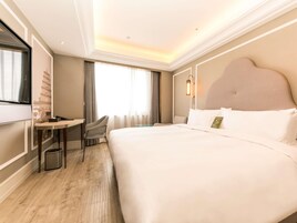 Quarto de hotel com cama grande, escrivaninha, cadeira, televisão e janela com cortinas.