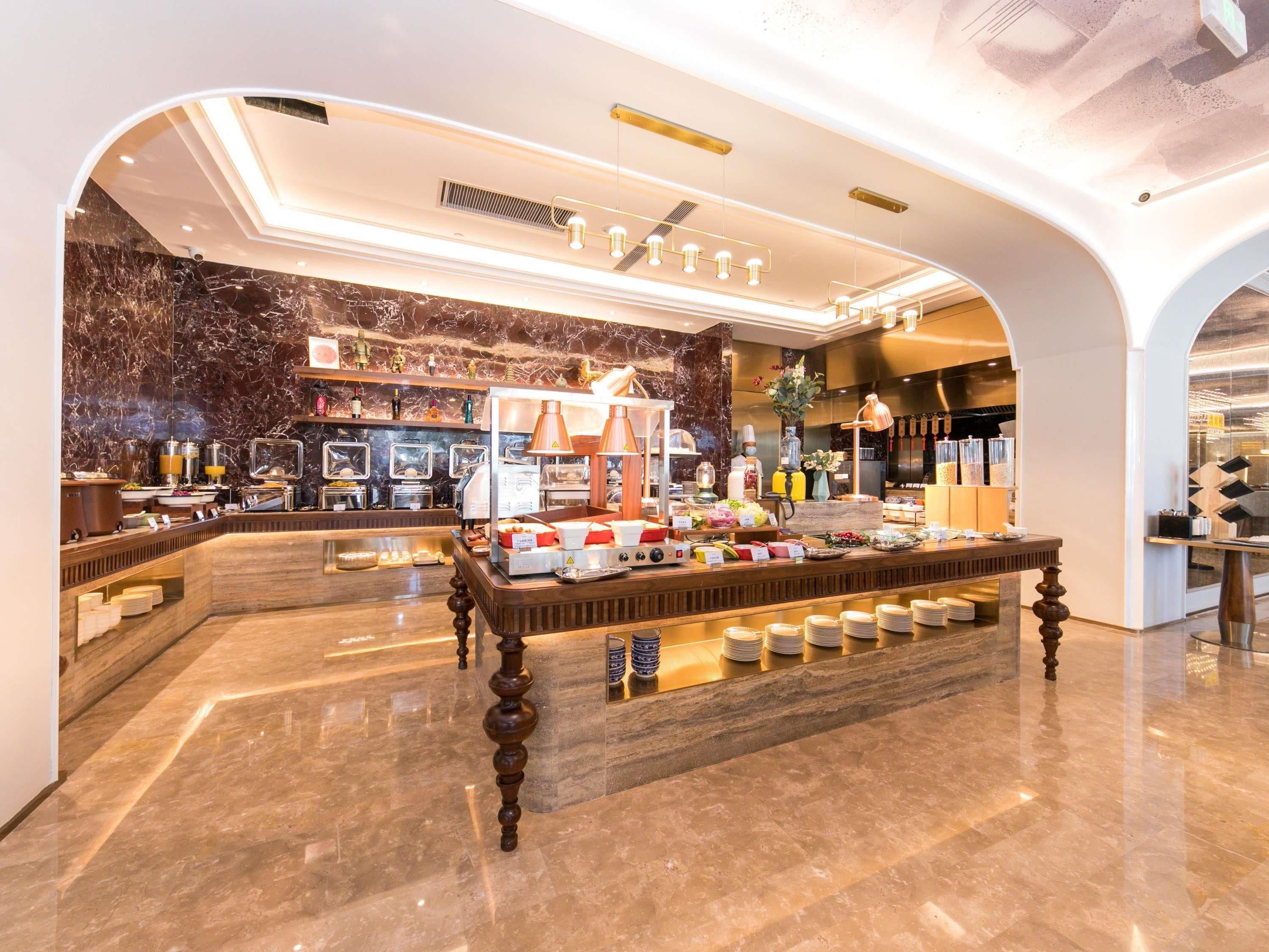 Um saguão de hotel com uma receção de mármore, zona de buffet e um candelabro moderno.