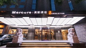 Entrada de hotel com fachada moderna, porta giratória e duas estátuas de leão na base.