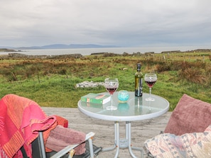 Uma mesa de vidro redonda com uma garrafa e duas taças, colocada num campo gramado com vista para o mar.