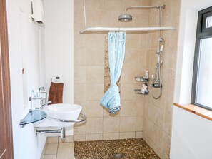Um banheiro com pia de vidro, chuveiro e porta-toalhas.