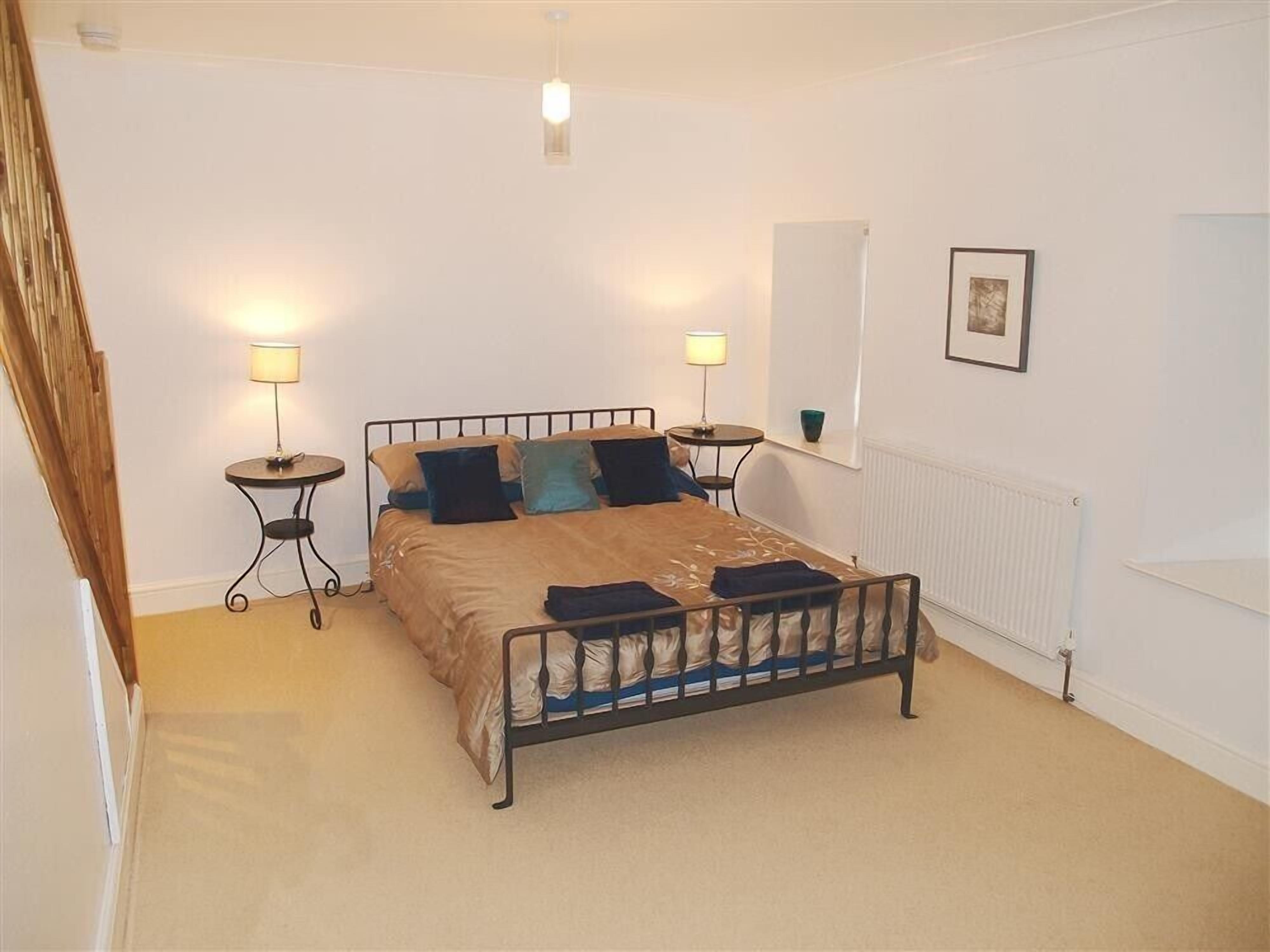 Quarto com cama, duas mesas de cabeceira, radiador e um quadro na parede.