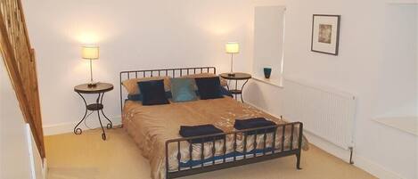 Quarto com cama, duas mesas de cabeceira, radiador e um quadro na parede.