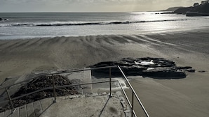 Uma praia com um corrimão de metal, ondas e céu claro.
